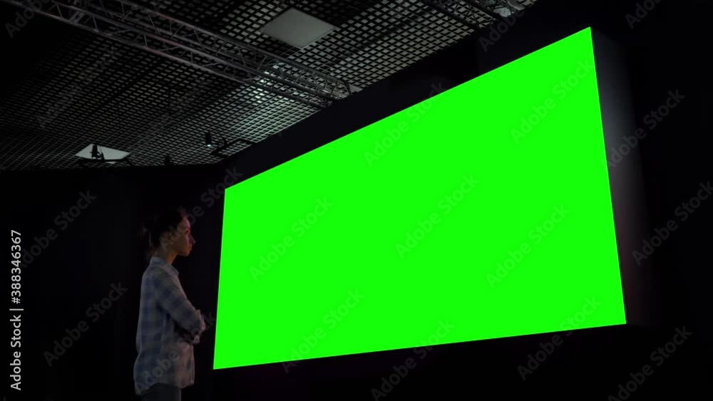 Woman looking at large wall blank interactive green display in dark ...