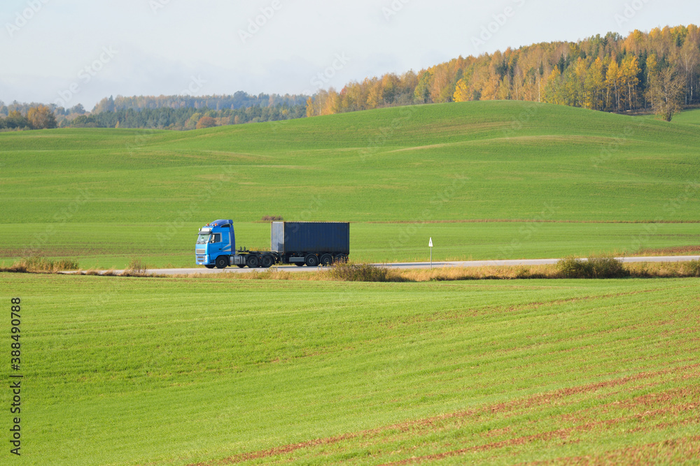 Modern semi-trailer truck riding through green plowed agricultural ...