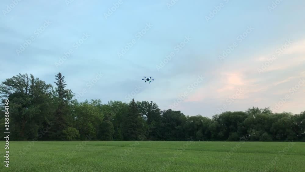 Six rotor drone copter flying over quiet grassy field with boreal tree ...