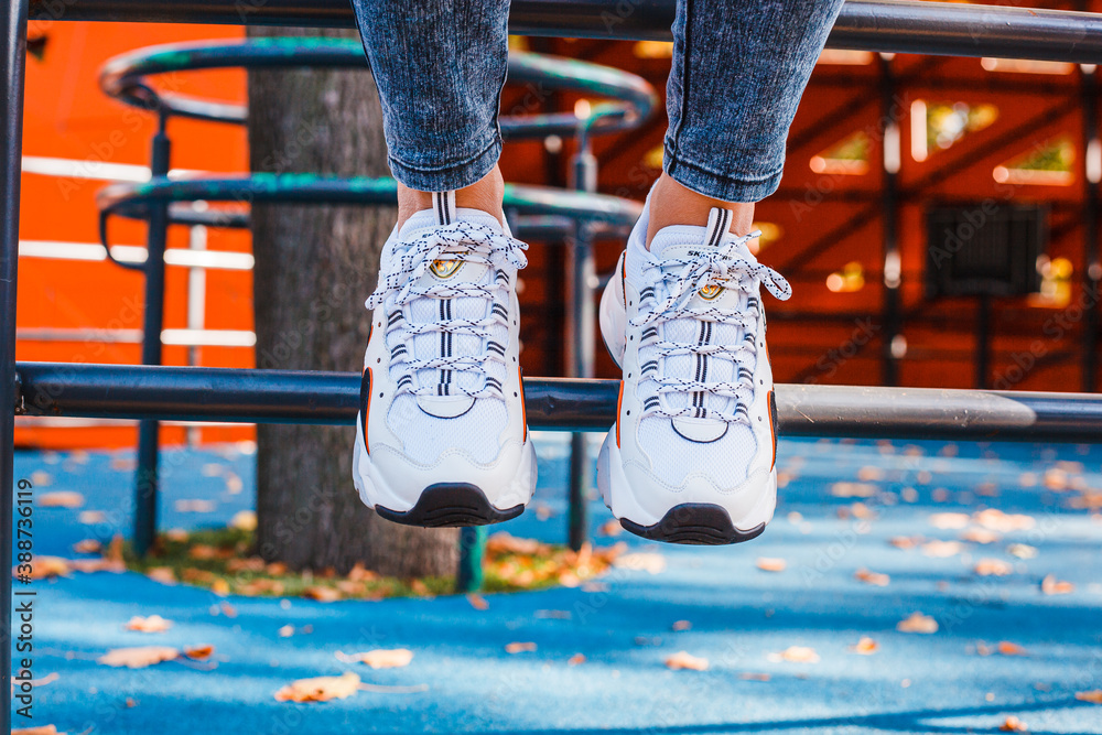 Legs of a girl in jeans and white sneakers with black inserts who sits ...