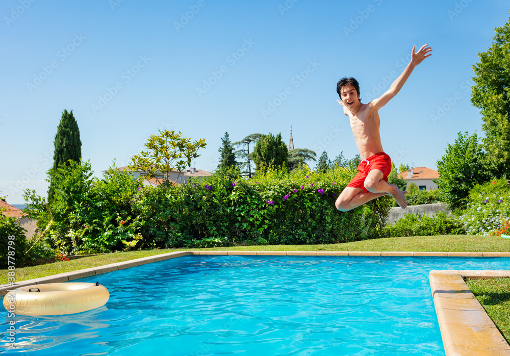 Teenage boy jump in mid air into the swimming pool view from side ...