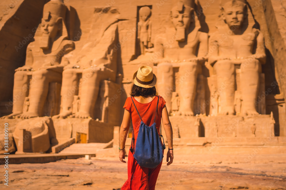A young tourist in red dress walking towards the Abu Simbel Temple in southern Egypt in Nubia ...