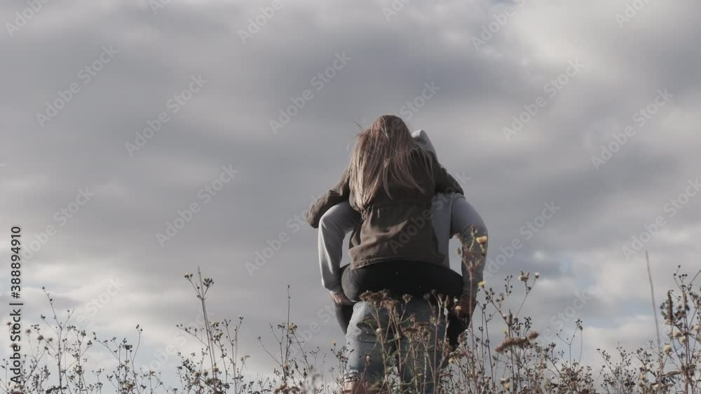 A girl jumps on a man from behind on a hump, holding on to his waist ...