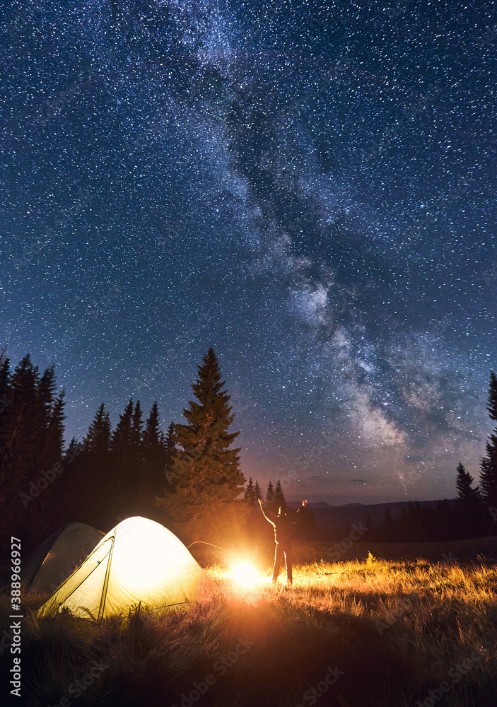 Night summer camping in forest. Back view male tourist raising hands ...