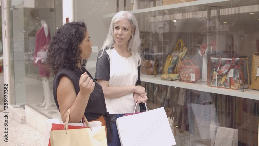 Relaxed positive customers with shopping bags standing and looking at ...