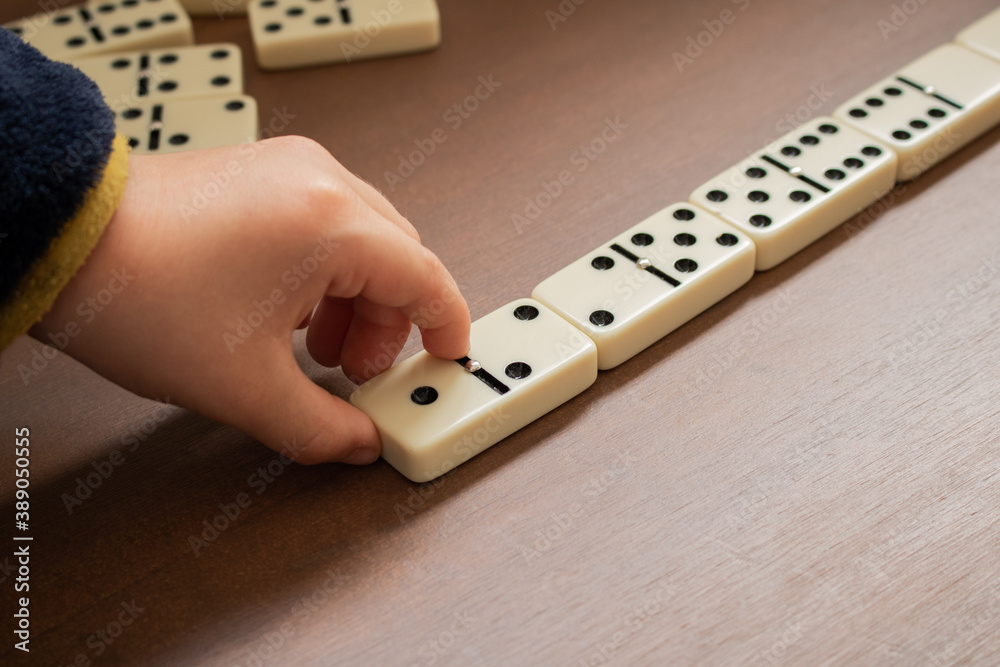Child playing dominoes on wooden table. Detail of child's hand and ...