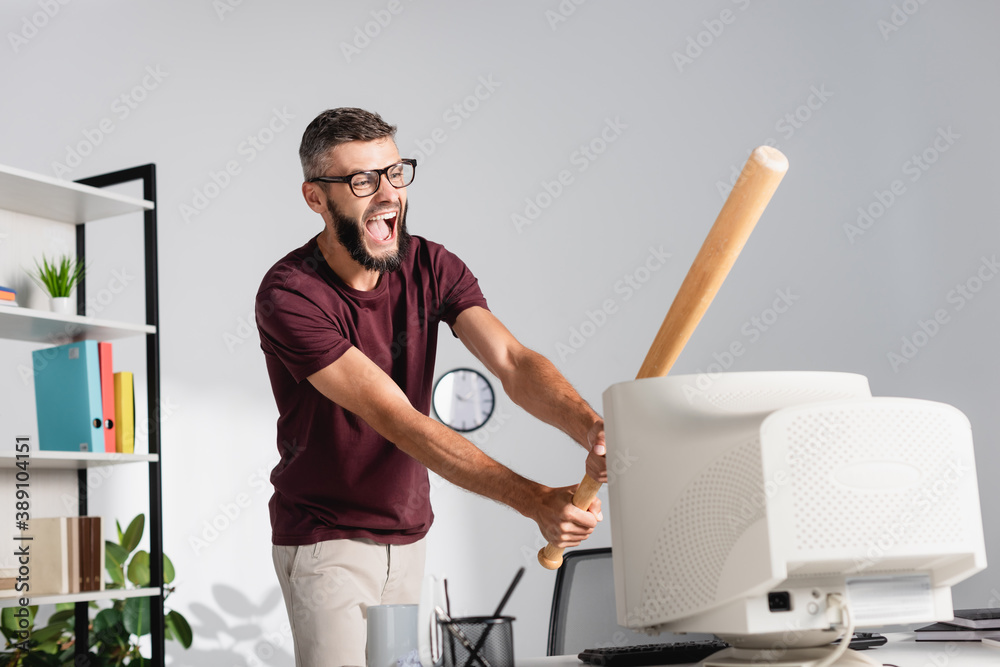 Screaming businessman beating computer monitor with baseball bat on ...