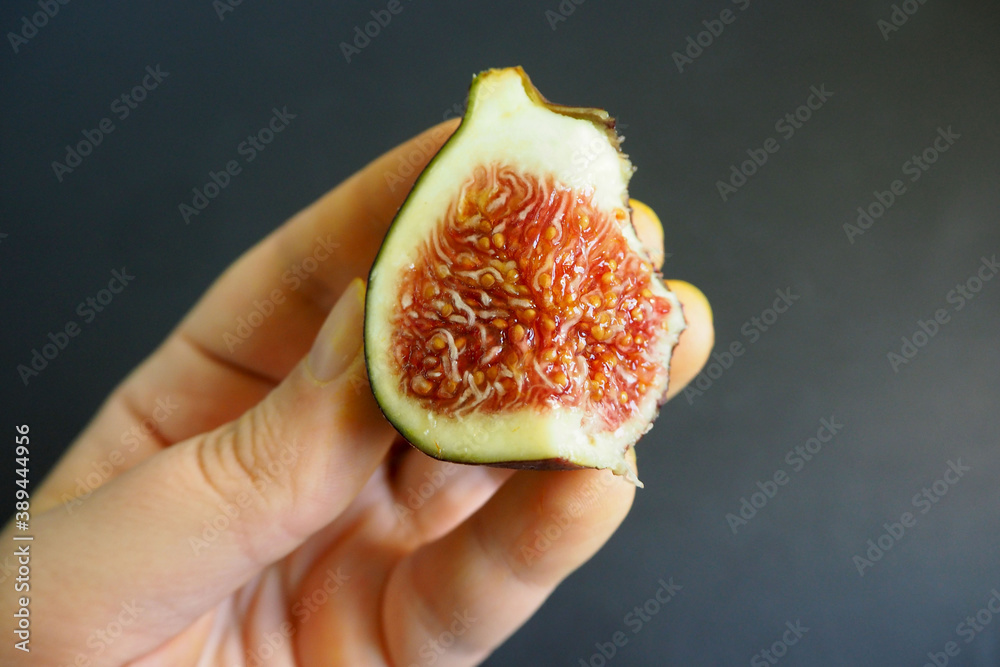 bitten juicy purple figs in a woman's hand on a black background side ...