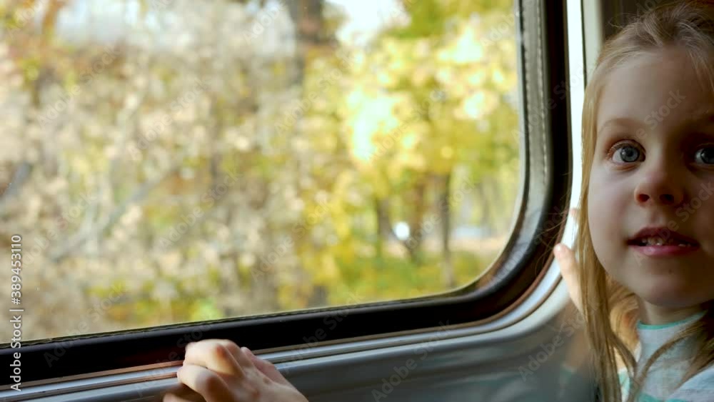 Vidéo Stock Cute little child girl smiles and looks out window of train ...