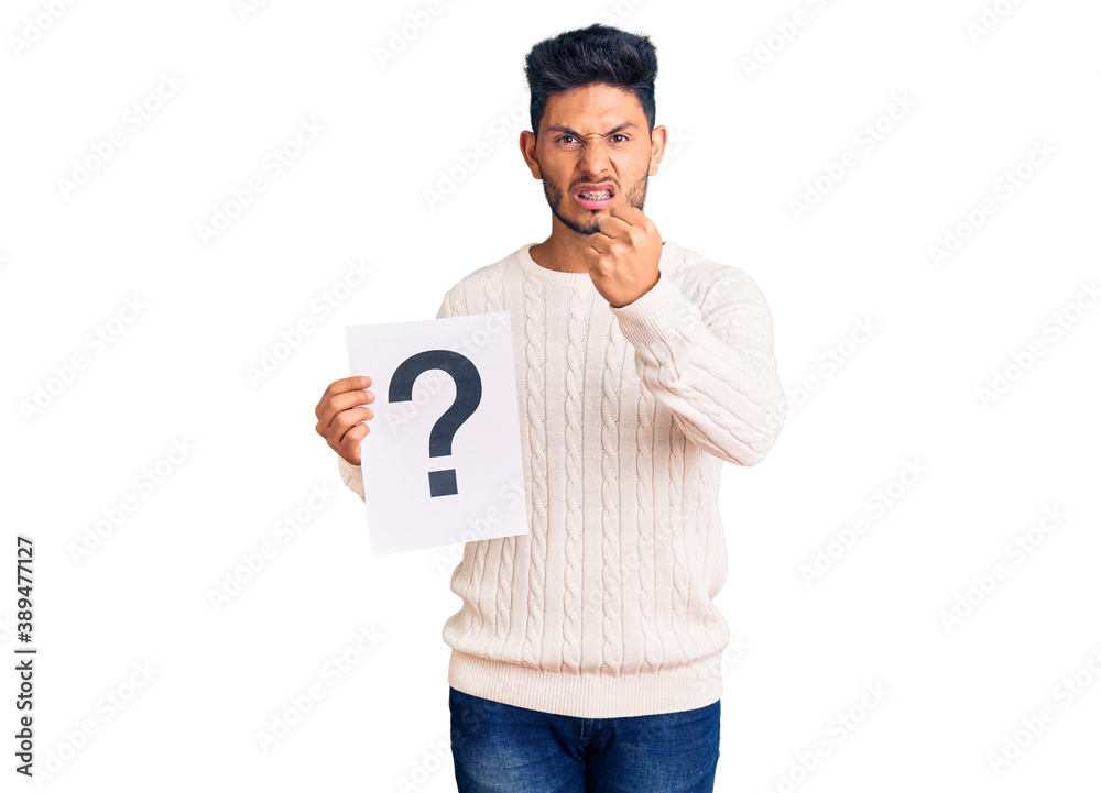 Handsome latin american young man holding question mark annoyed and ...