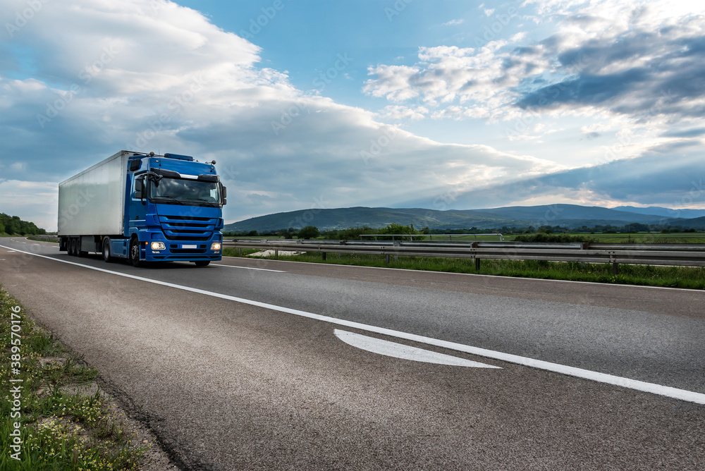 Blue semi trailer truck on a highway driving at bright sunny sunset ...