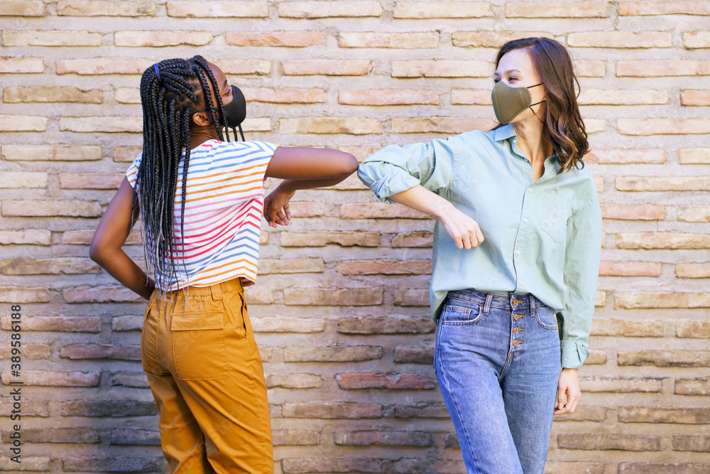 Multiethnic young women wearing masks greeting at each other with their ...