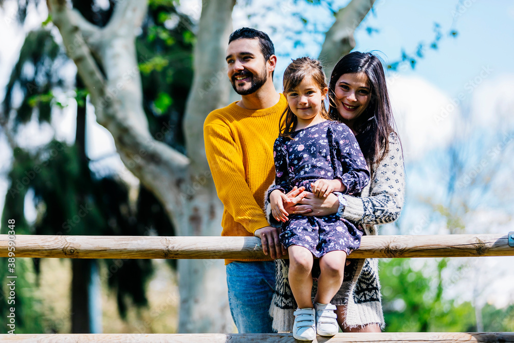Happy family standing in the park while little girl looking at camera ...