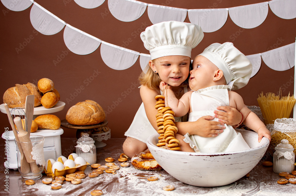 two little girls sisters in chef costumes in the studio with bakery ...