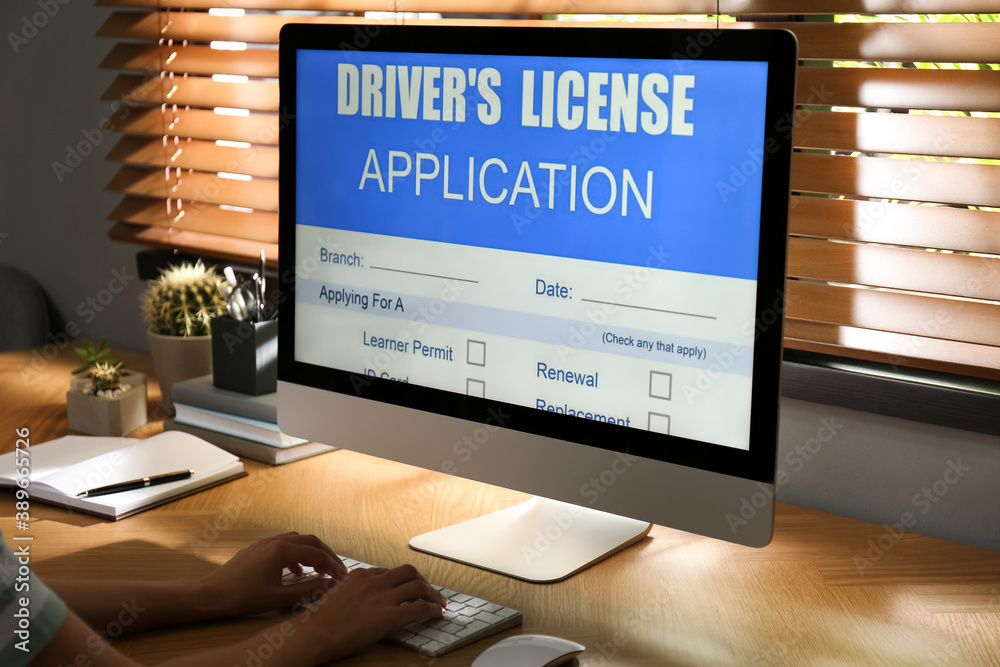 Woman using computer to fill driver's license application form at table ...