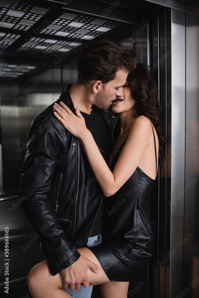 Man In Leather Jacket Kissing And Holding Leg Of Seductive Woman In