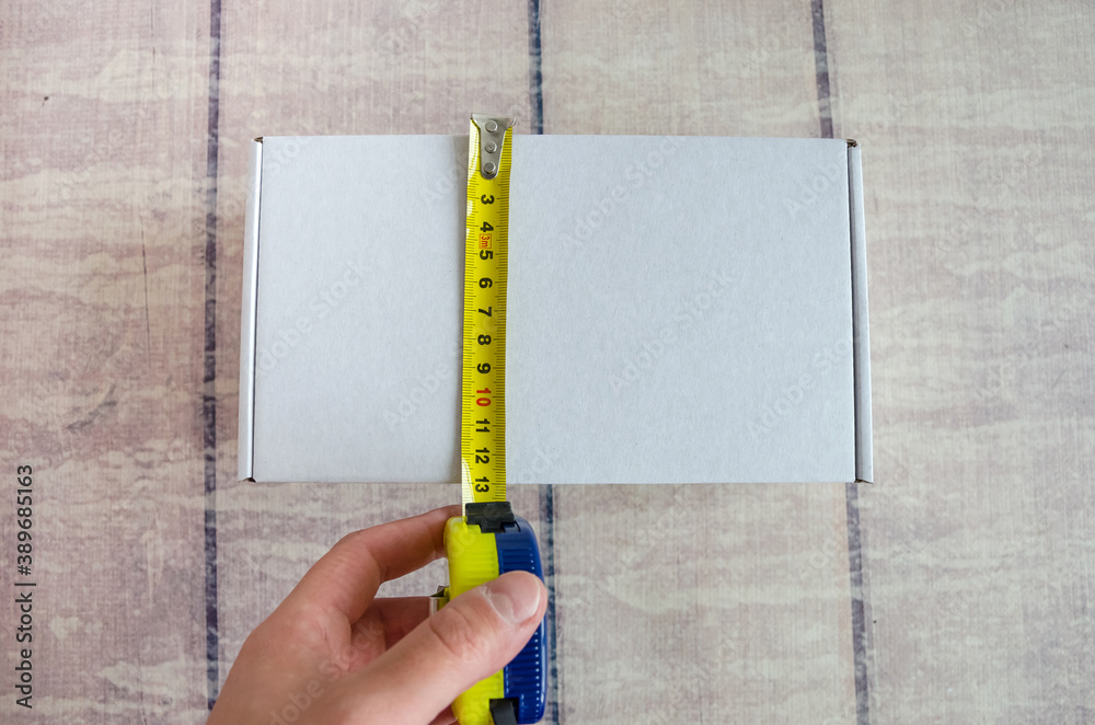 Worker's hand using a tape measure measures cardboard boxes. Shopping ...