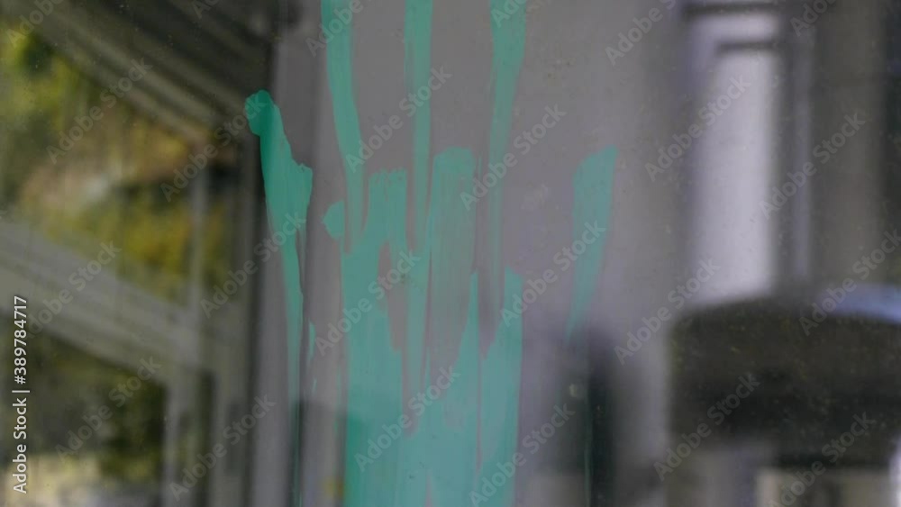 A hand smears green paint on a window glass, view from outside, slight ...