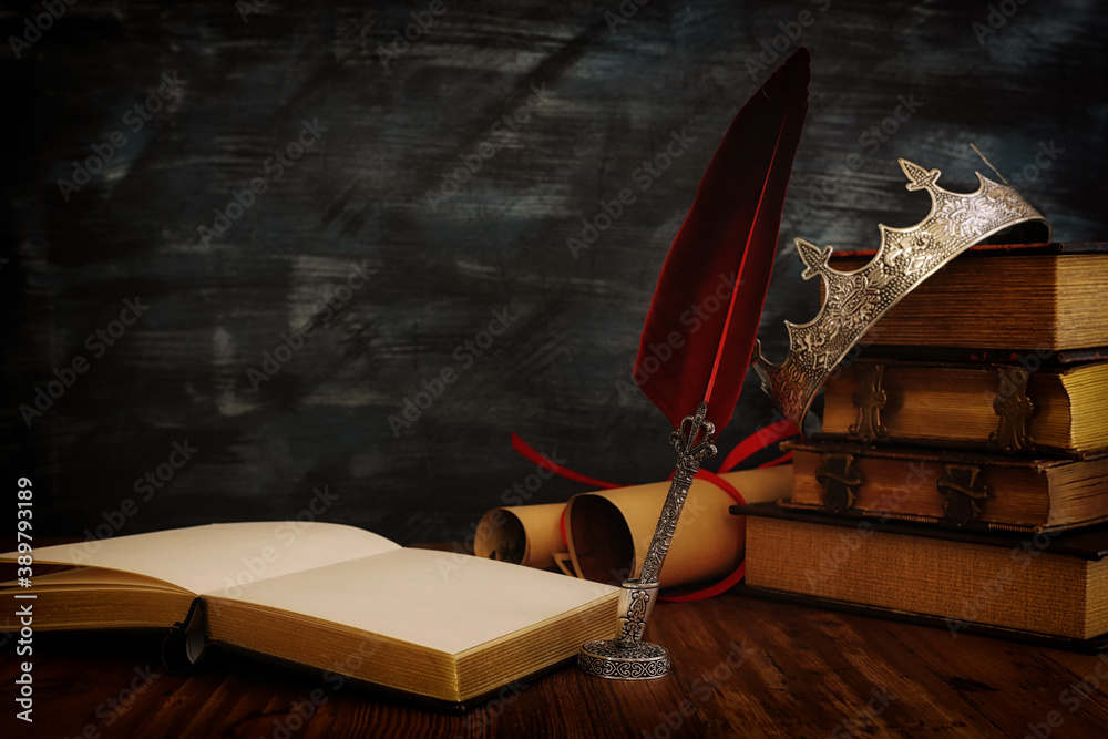 low key image of beautiful queen/king crown, old books and feather ...