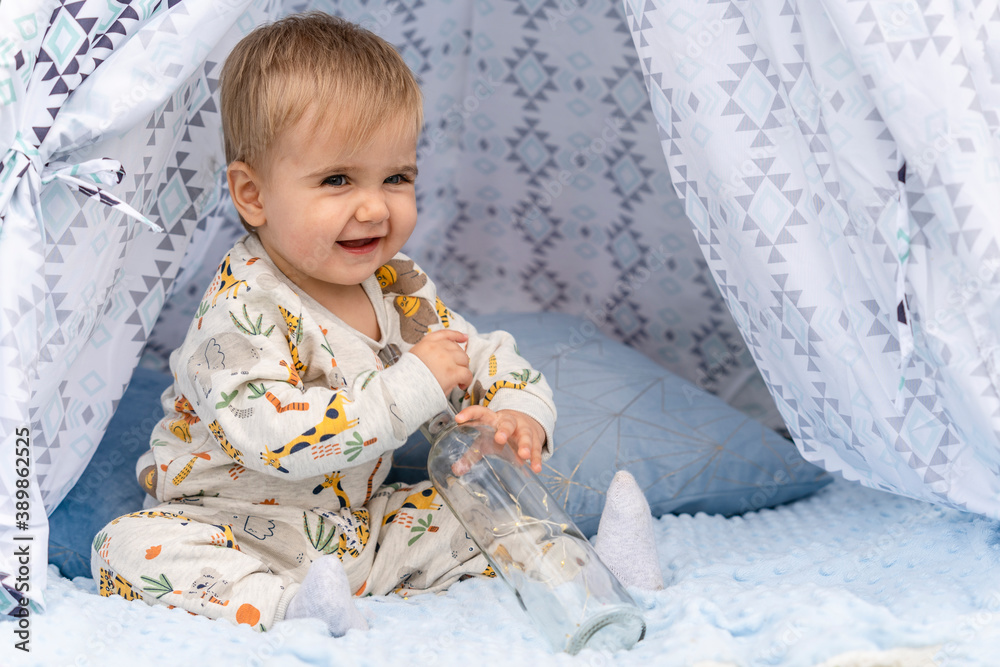 blond baby with blue eyes of a few months sitting inside a teepee tent ...