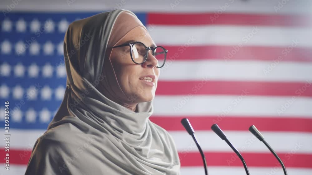 Muslim female politician in hijab and glasses standing by rostrum and ...