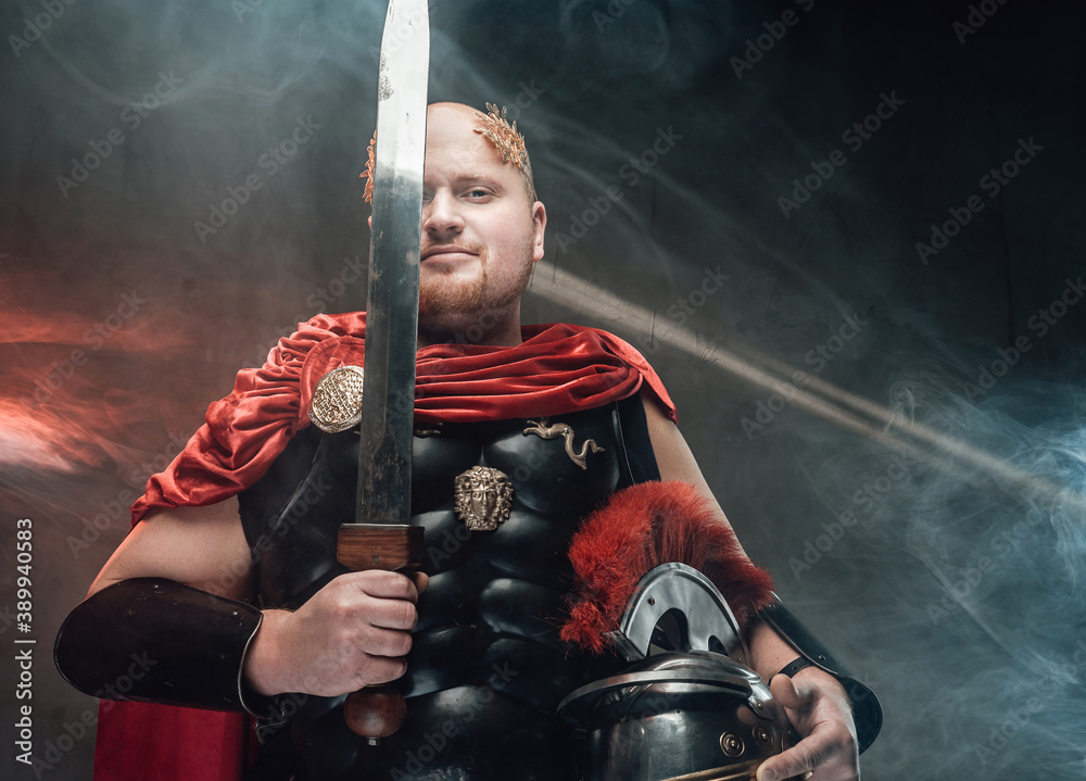 Handsome hairless roman soldier in dark armour and red cape poses ...