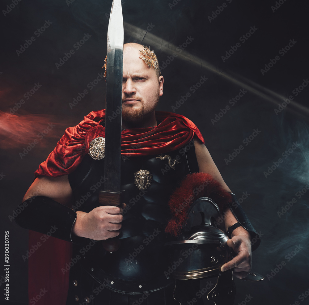 Handsome hairless roman soldier in dark armour and red cape poses ...
