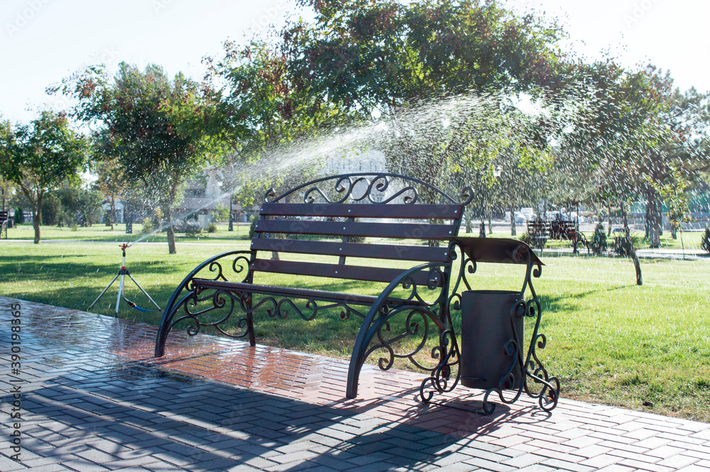 A park bench on a green lawn wet from the spray of water from the lawn ...