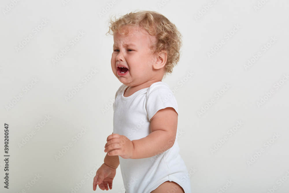 Cute baby boy standing against white wall and cries, having bed ...