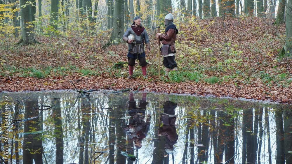Medieval Vikings talking in the forest near lake reflected in water ...