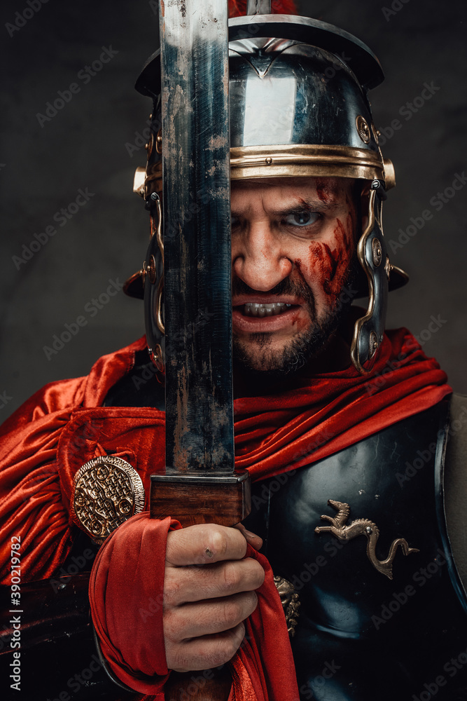 Savage roman barbarian with blood on his face looks at camera holding ...