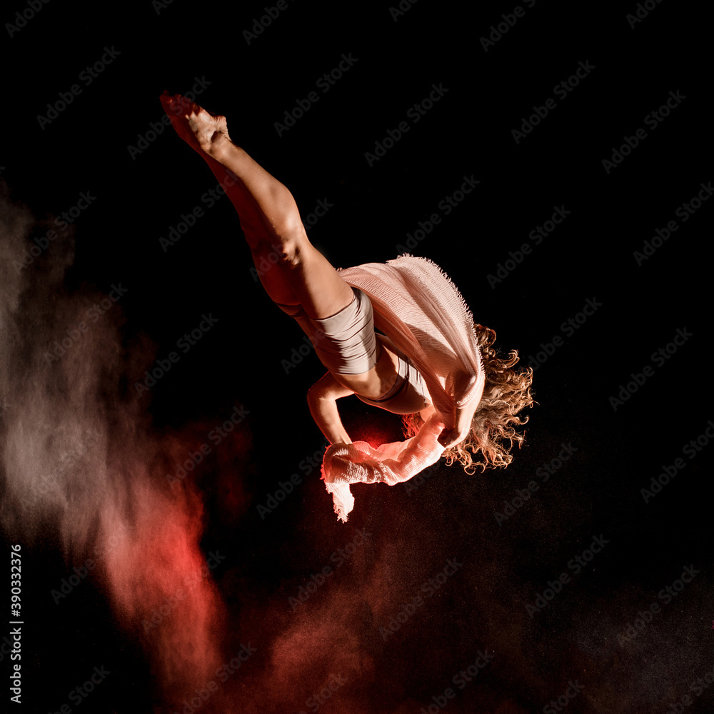 Beautiful young female athlete flying upside down outdoor at dark time ...