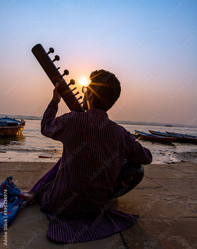 a man playing sitar at bank of ganges river at varanasi and beautiful ...