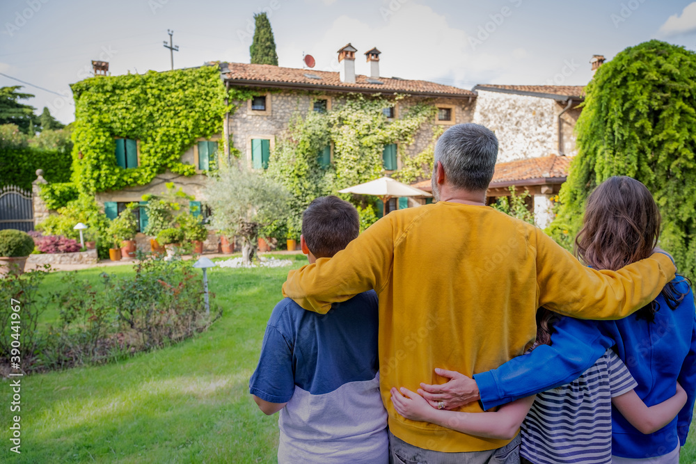 Back view of happy family hugging is standing outside their new house ...