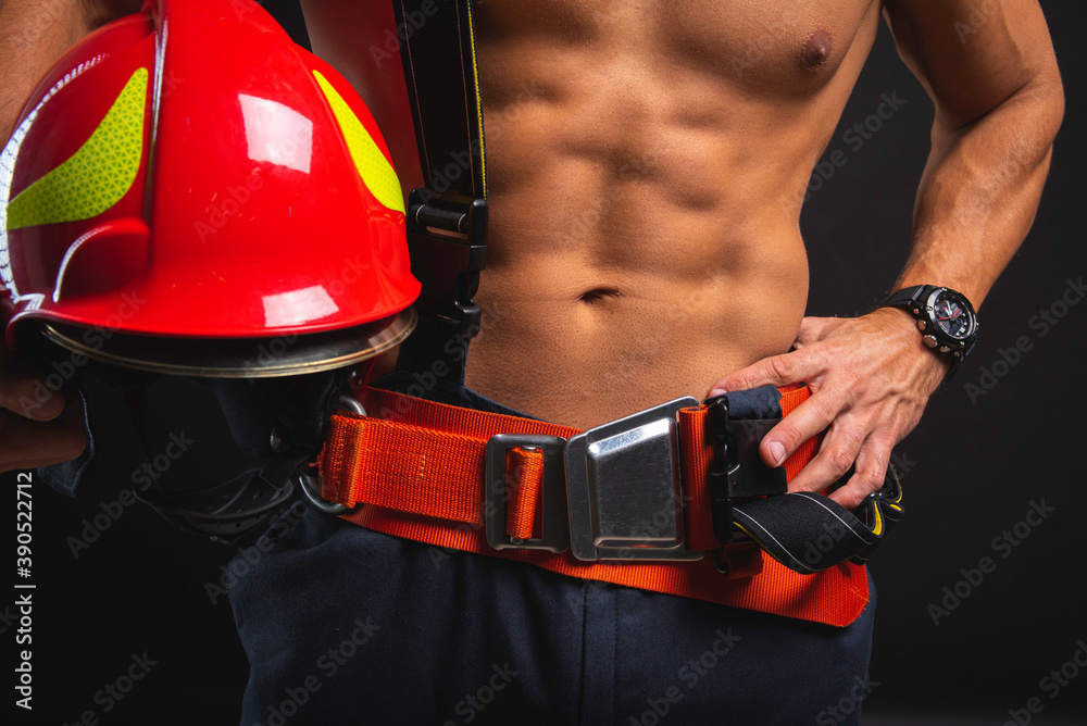 muscular, handsome young firefighter on dark background holding fire ...