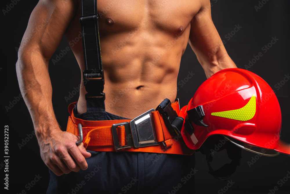muscular, handsome young firefighter on dark background holding fire ...