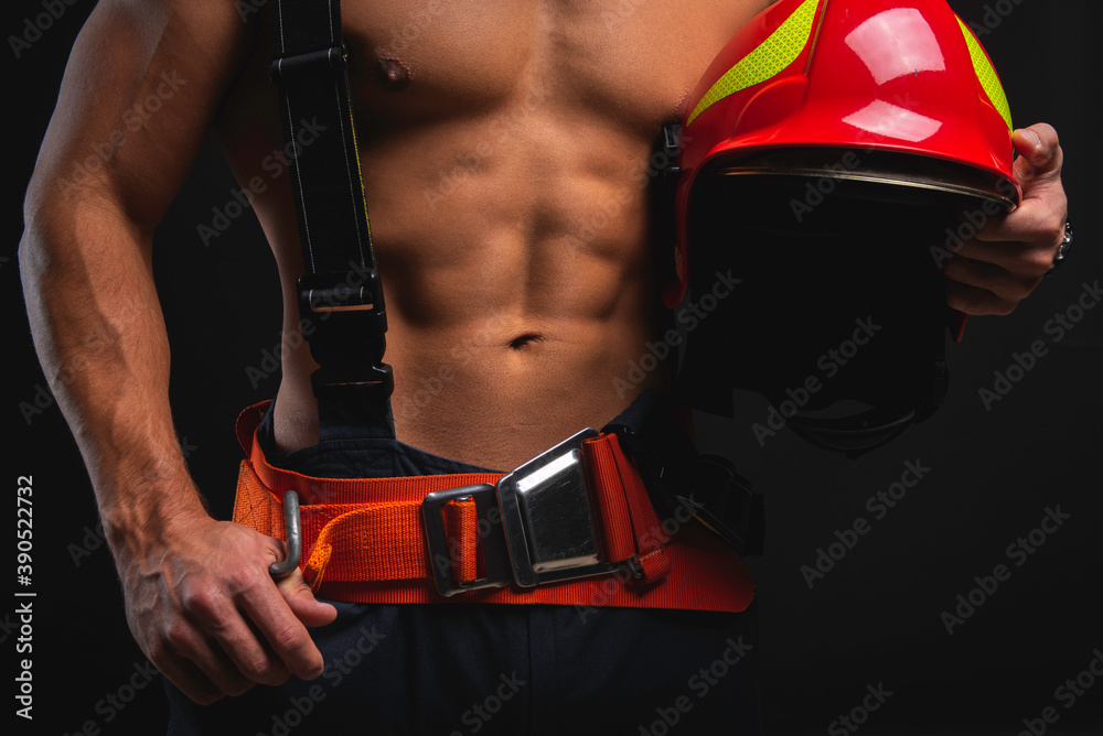 muscular, handsome young firefighter on dark background holding fire ...