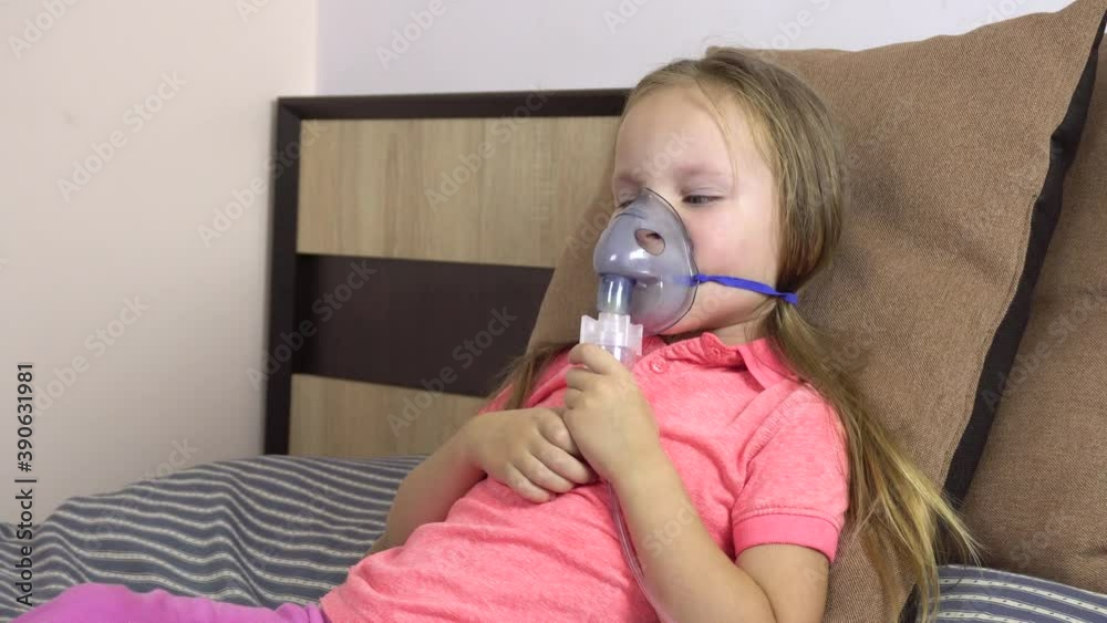 A little girl makes inhalation with a nebulizer while lying in bed ...