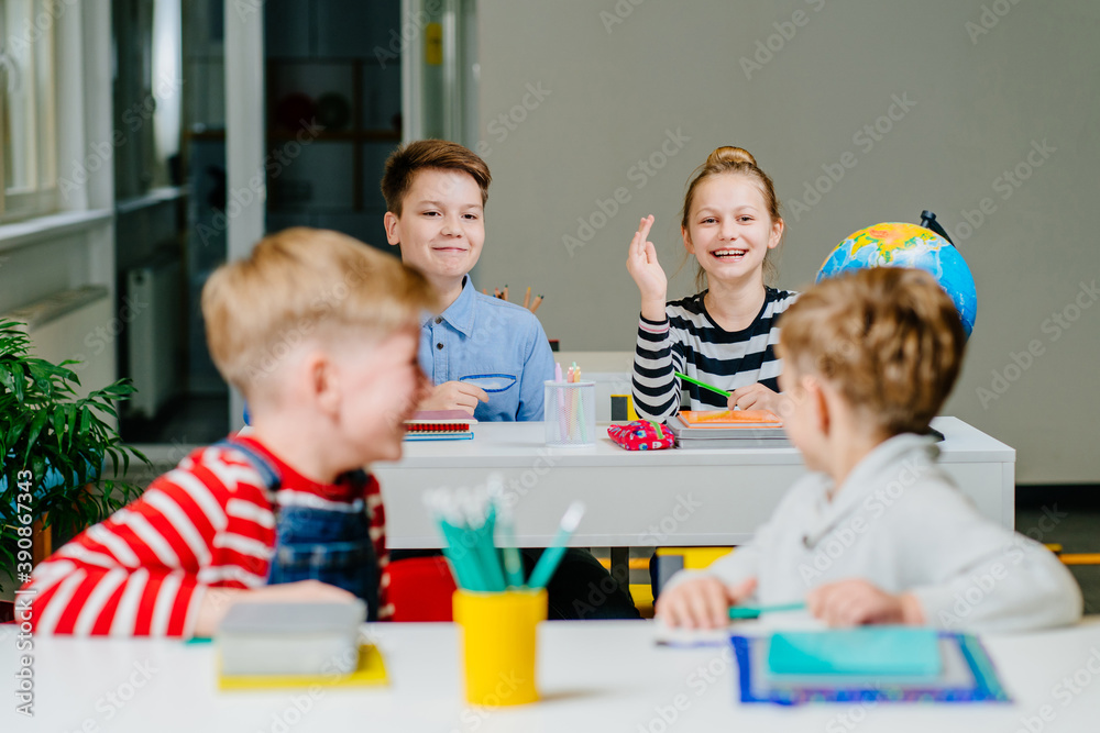 Four happy children in classroom. Smiling female pupil raised hand ...