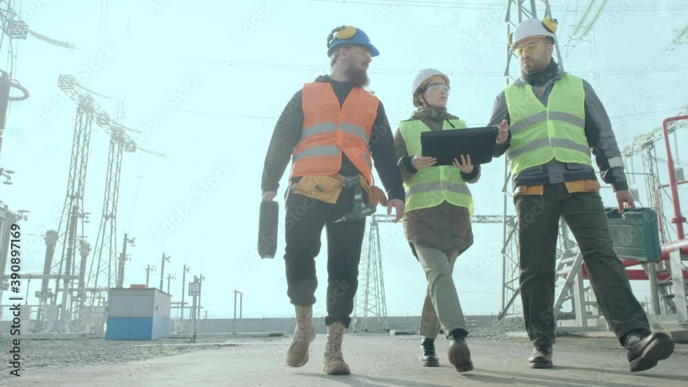 A team of energy engineers, two men and a woman in overalls, helmets ...