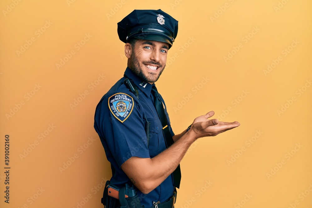 Handsome hispanic man wearing police uniform pointing aside with hands ...