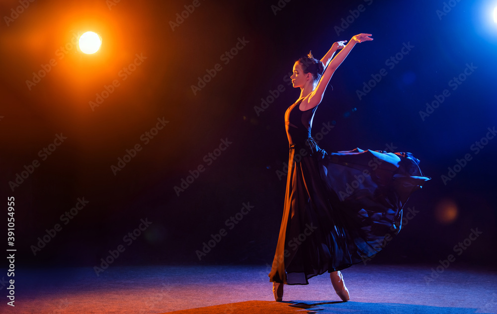 Ballerina in a black dress and crown is dancing on black background ...