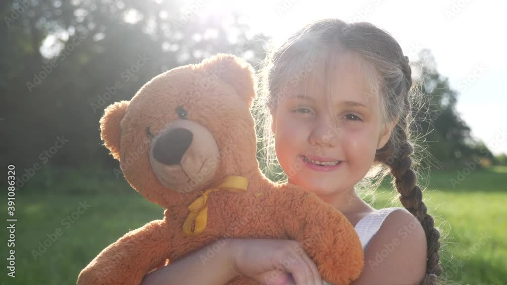 little kid girl hugging a teddy bear toy portrait in the park in nature ...