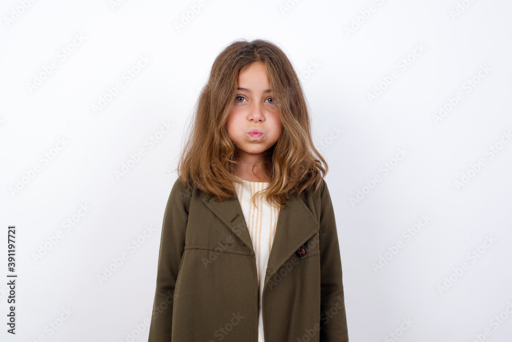 Beautiful little girl standing against white background, puffing cheeks ...