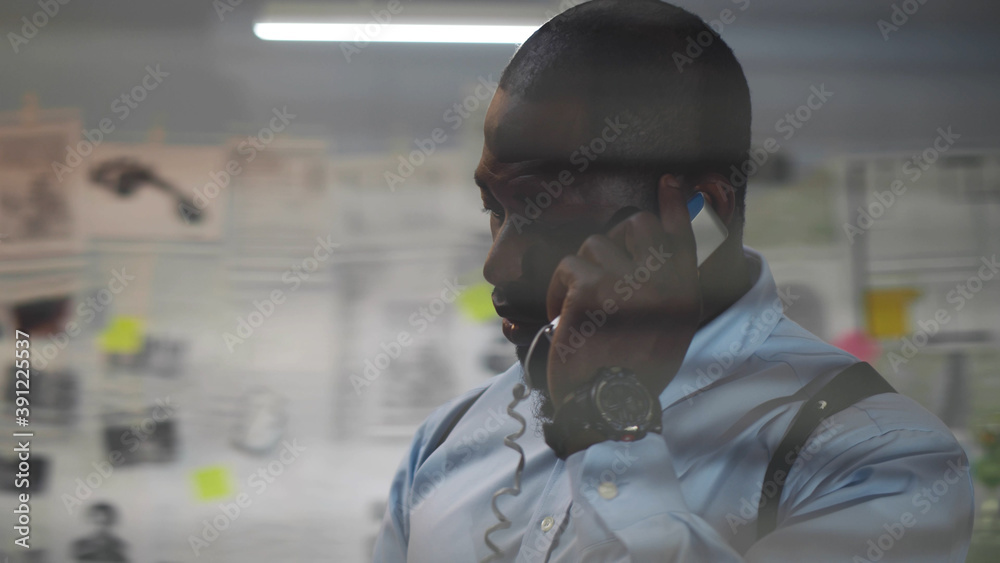 View through window louvers of afro policeman talking on phone during ...
