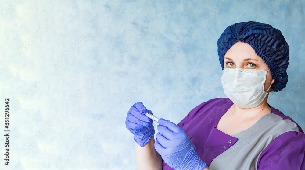 Blue-eyed nurse in overalls and personal protective equipment on a blue ...