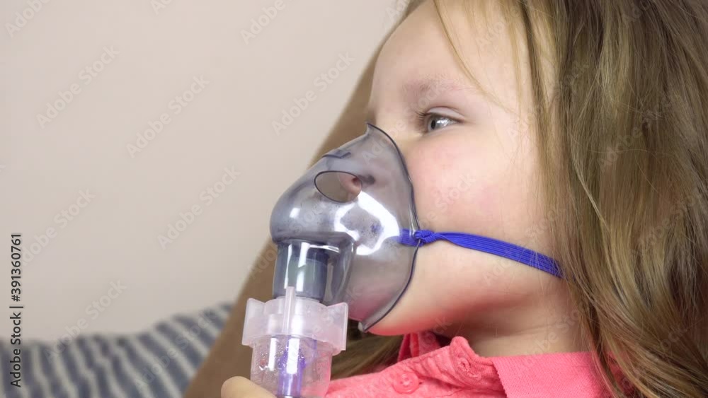 A little girl makes inhalation with a nebulizer while lying in bed ...