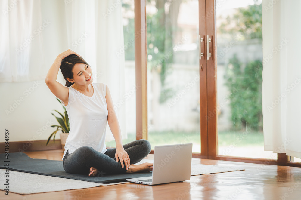 Smiling Asian woman doing yoga neck stretching online class from laptop ...