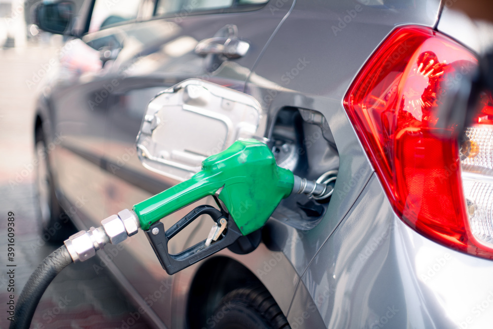 Man at a petrol pump fuel station inserting nozzle into fuel tank of a ...