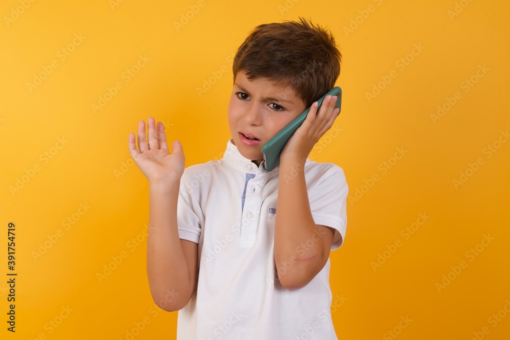 Young handsome Caucasian little boy standing against yellow, talking on ...